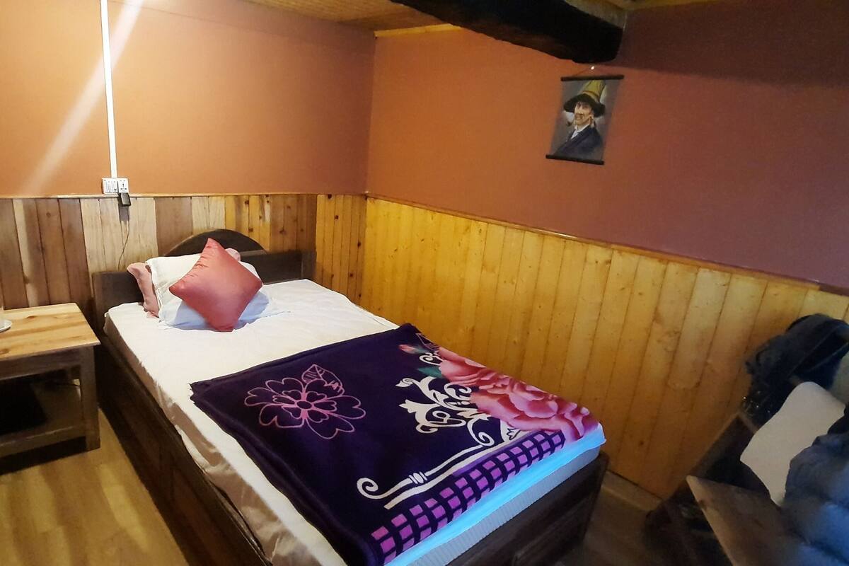 Um quarto pequeno e acolhedor, com uma cama, um criado-mudo, uma cadeira e painéis de parede de madeira.