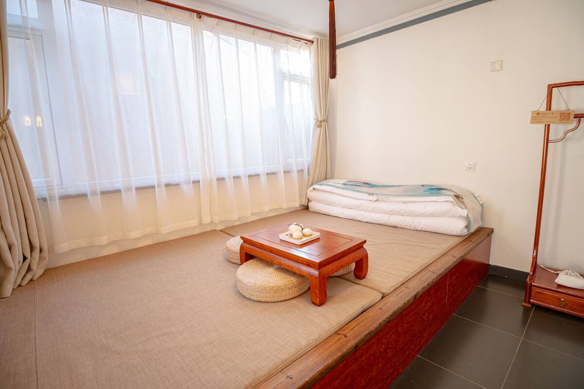 Quarto com cama futon, mesa de madeira com bandeja e assento futon.