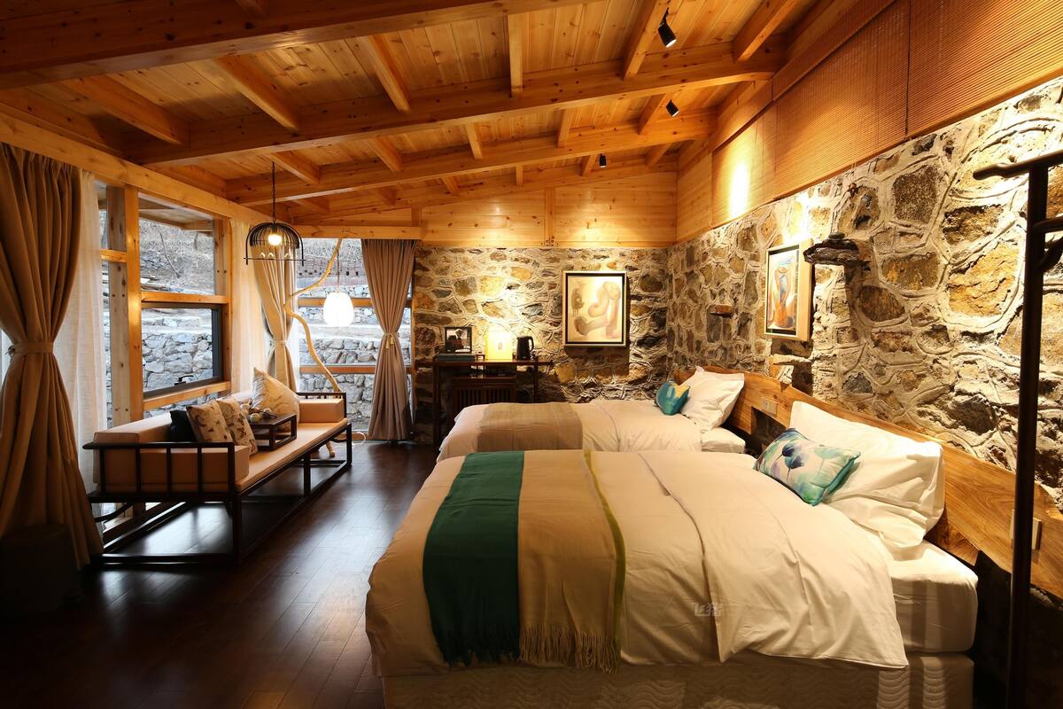 Quarto aconchegante com parede de pedra, teto de madeira e cama com manta verde.