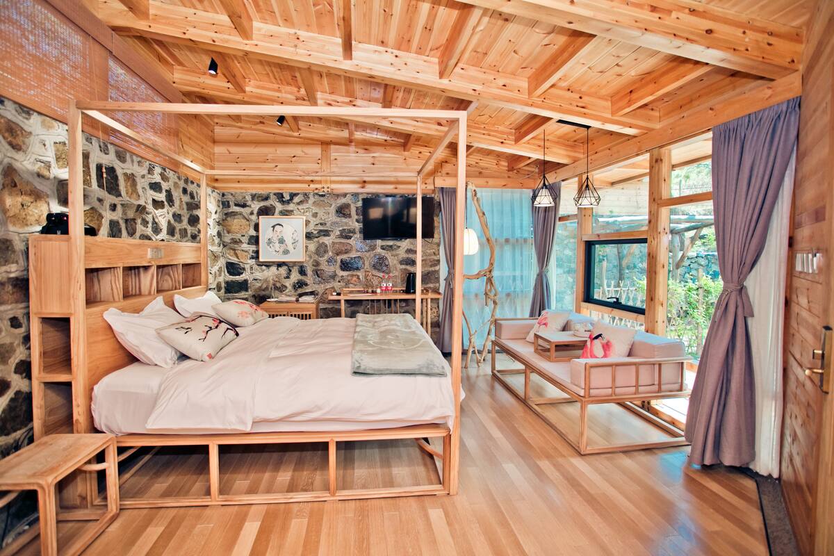 Interior de uma cabana de madeira com uma cama, uma mesinha e um espaço de estar.