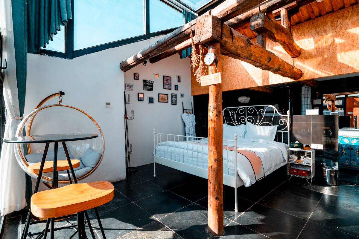 Quarto moderno com cama, cadeira suspensa e uma mesinha.