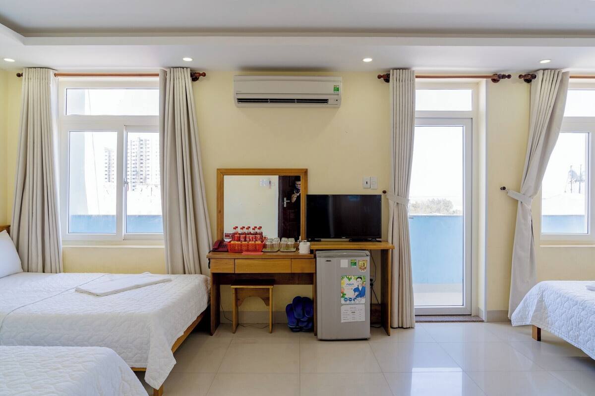 Quarto de hotel com duas camas, uma escrivaninha, televisão, frigorífico e janela com cortinas.