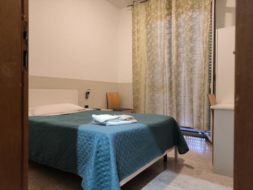 Quarto com cama, mesa de cabeceira, luminária e janela com cortinas.
