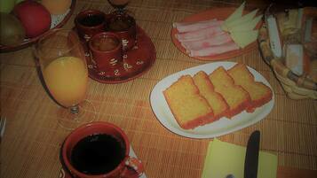 Uma mesa de café da manhã com pão, um copo de suco de laranja e uma xícara de café sobre um tapete de bambu.