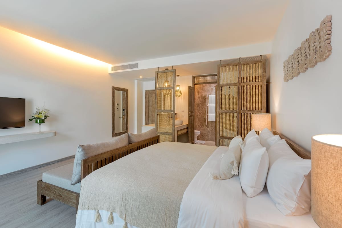 Quarto de hotel moderno com uma cama grande, uma televisão presa à parede e um banco de madeira.