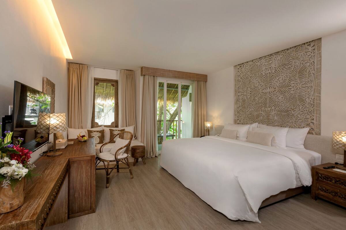 Quarto de hotel espaçoso com uma cama grande, uma escrivaninha de madeira, uma cadeira e uma televisão.