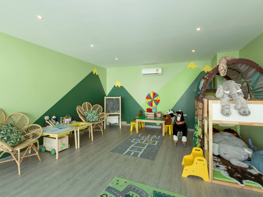 Uma sala de brinquedos infantil com parede verde, mesa de brincar de madeira e uma cama beliche com bichos de pelúcia.
