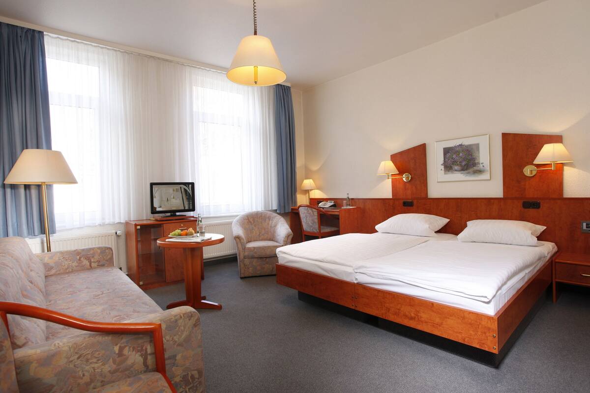 Quarto de hotel com uma cama grande, uma mesa de escritório com um computador, uma cadeira e uma televisão.