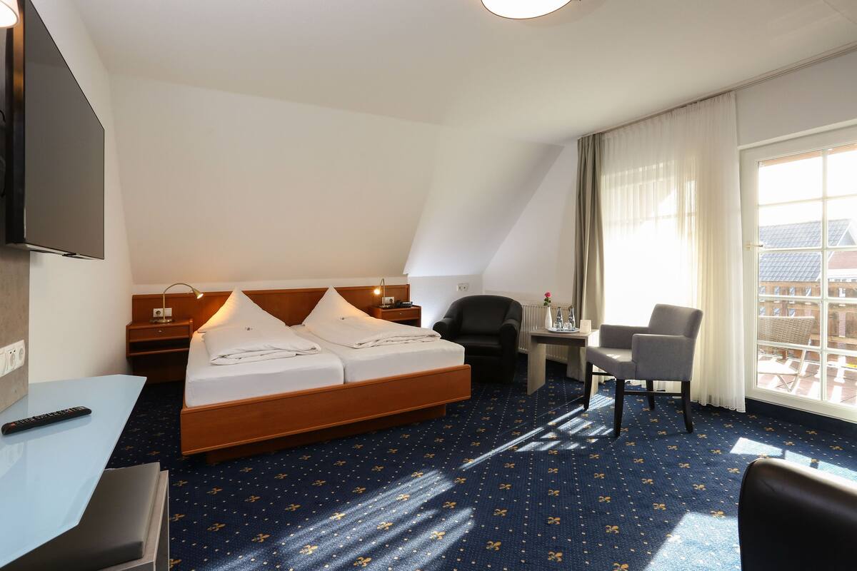 Quarto de hotel com uma cama, uma escrivaninha, uma cadeira e uma televisão.