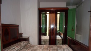 Quarto com cama, guarda-roupa de madeira, porta verde e radiador.