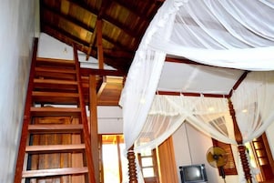 Quarto com escada de madeira, cama com dossel e televisão.