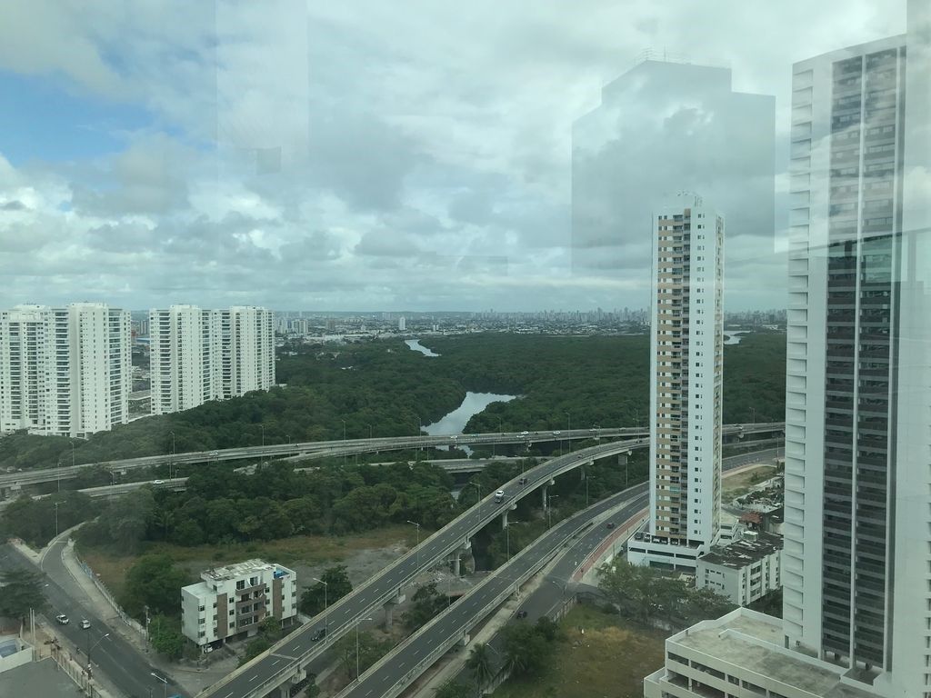 Um edifício alto com vários andares, cercado por vegetação e um rio ao fundo.