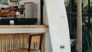 Uma área de bar com uma prancha de surf encostada na parede, uma máquina de café e uma cadeira.