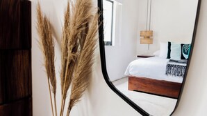 Quarto com um espelho grande refletindo o ambiente, um guarda-roupa de madeira e grama de pampa.