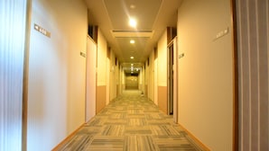 Um corredor de hotel com piso coberto de carpete, portas em ambos os lados e luminárias no teto.