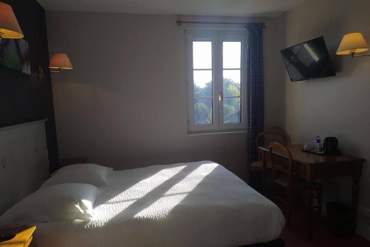 Quarto de hotel com cama, escrivaninha, cadeira, televisão e janela com cortinas.