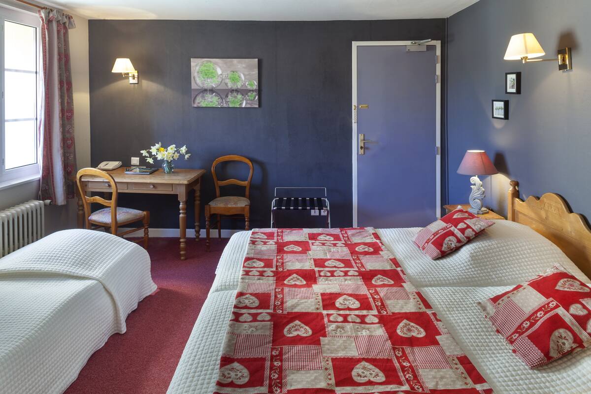 Quarto de hotel com cama, duas cadeiras, escrivaninha e radiador.