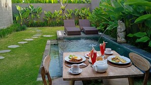 Uma área de refeições com piscina, assentos externos e vegetação exuberante.