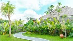 Um caminho sinuoso que leva a um edifício com telhado de colmo, rodeado por vegetação exuberante e plantas grandes.