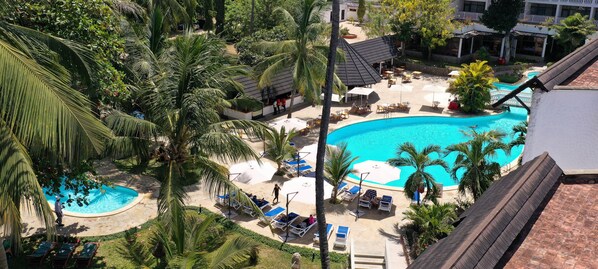 Um resort com uma piscina central grande, piscinas menores e áreas de estar ao ar livre rodeadas por palmeiras.