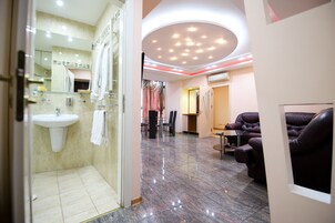 Um hall de hotel moderno com chuveiro em cabine de vidro, área de estar com poltronas de couro e um balcão de recepção.