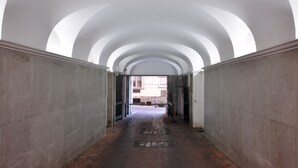 Um corredor com teto abobadado, que leva a uma área aberta com um edifício ao fundo.