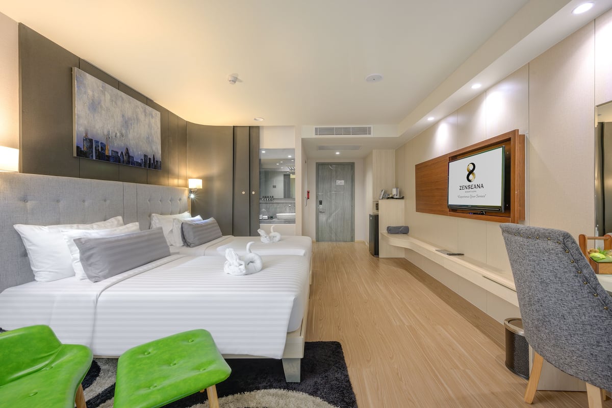 Quarto de hotel moderno com uma cama grande, duas mesas de cabeceira, uma TV de tela plana, uma escrivaninha com cadeira e um banheiro visível por uma porta aberta.