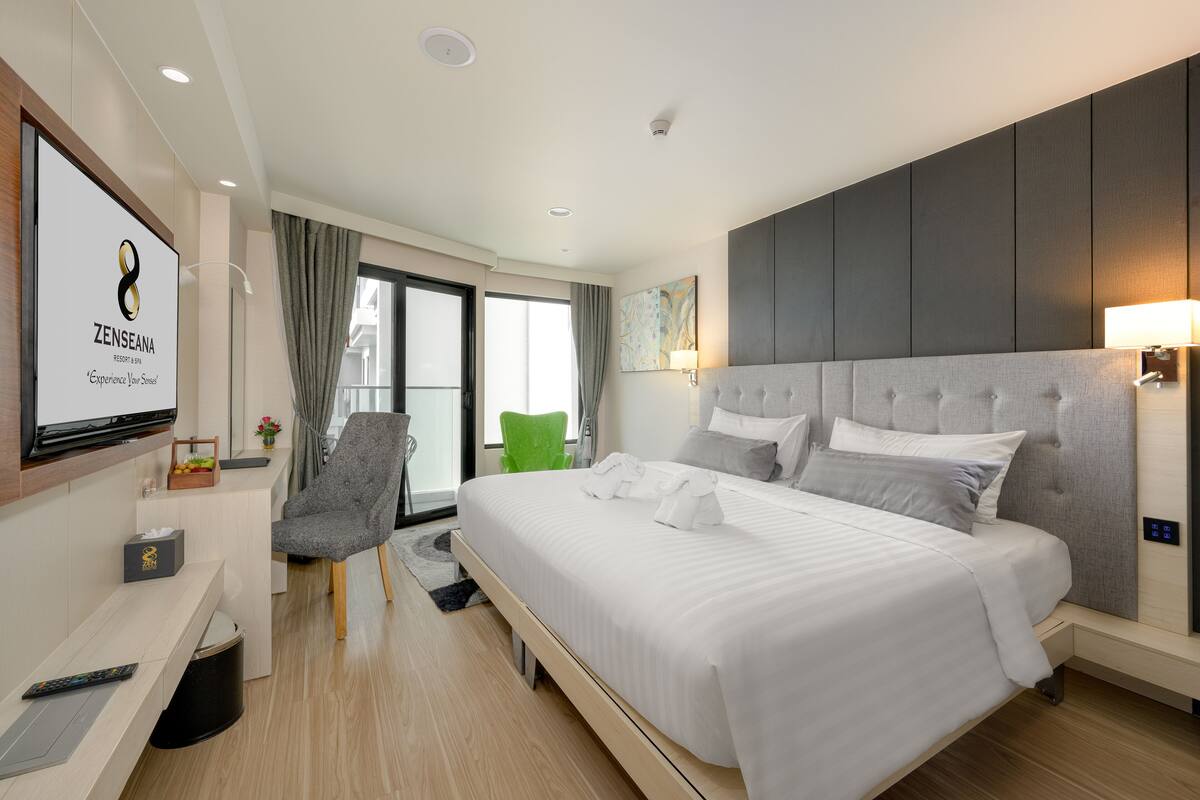 Quarto de hotel moderno com uma cama grande, televisão, escrivaninha e uma cadeira verde.