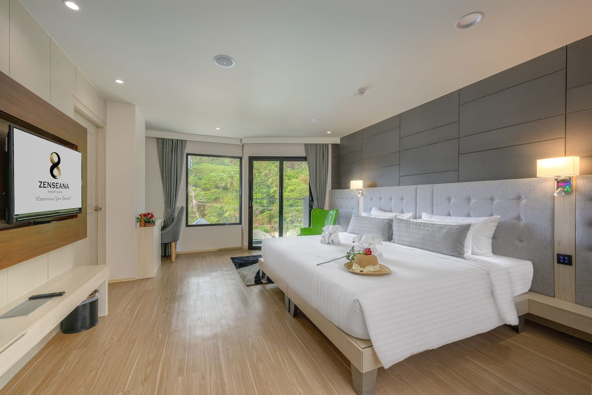Quarto de hotel moderno com uma cama grande, TV fixada na parede e vista para o verde lá fora.