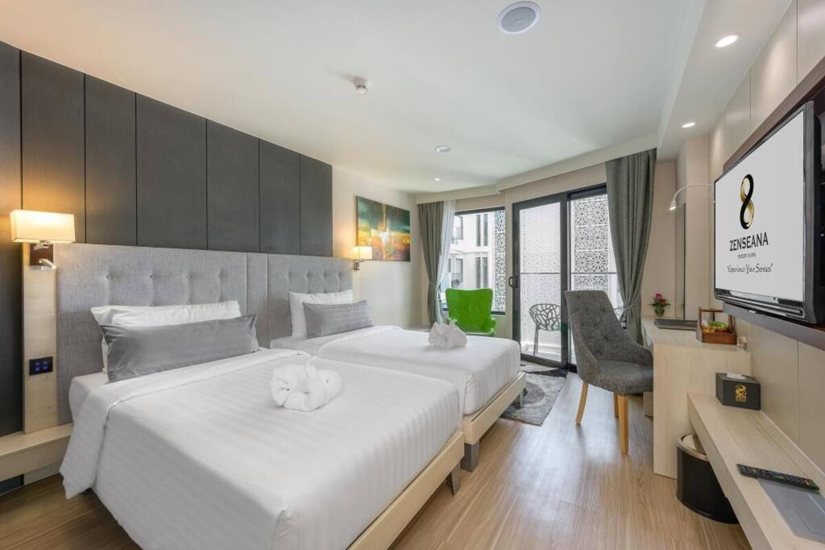 Quarto de hotel com duas camas, uma escrivaninha, uma cadeira, televisão e varanda com vista.