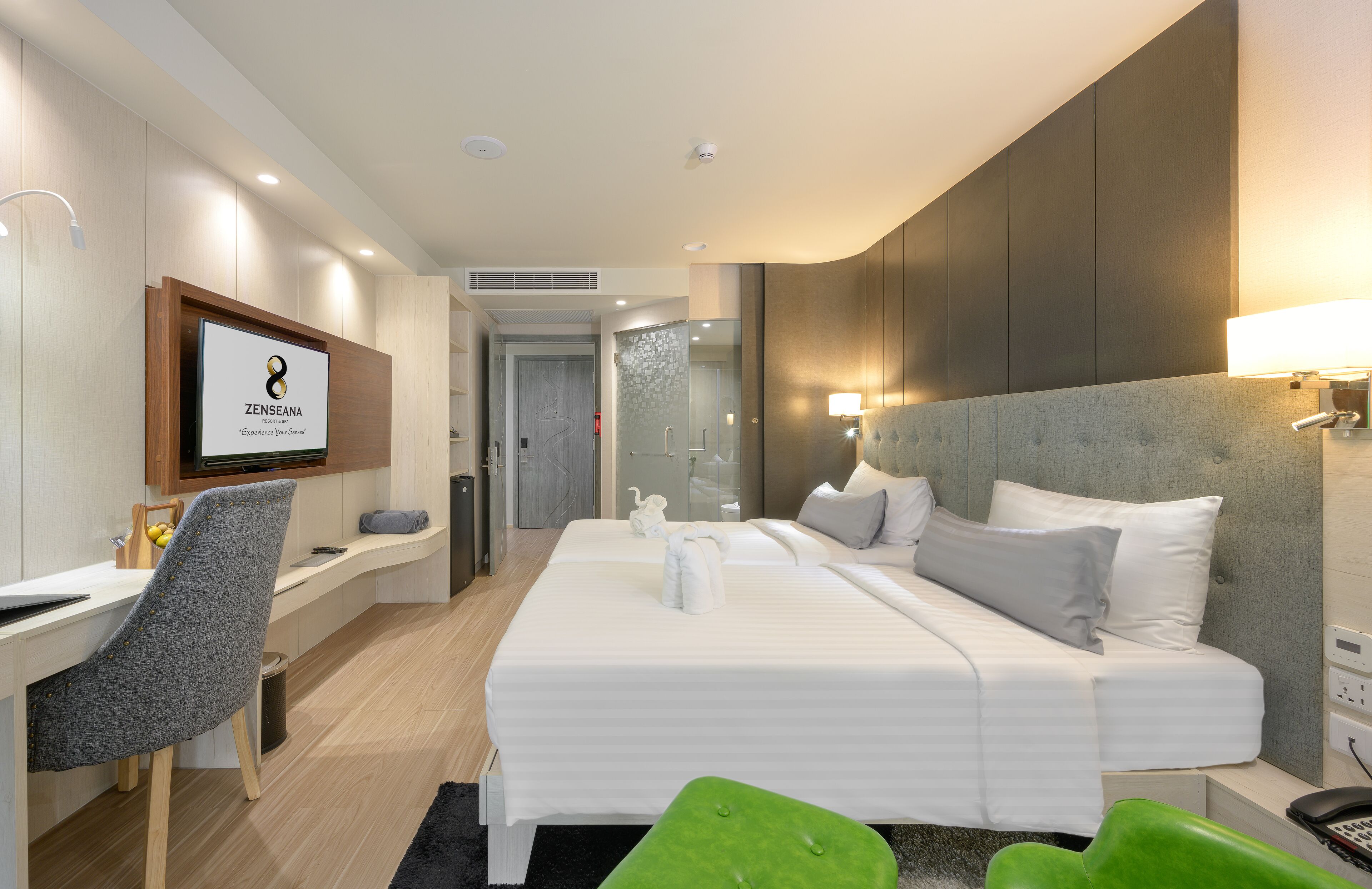 Quarto de hotel moderno com uma cama grande, uma escrivaninha, uma cadeira, uma televisão e um banheiro visível ao fundo.