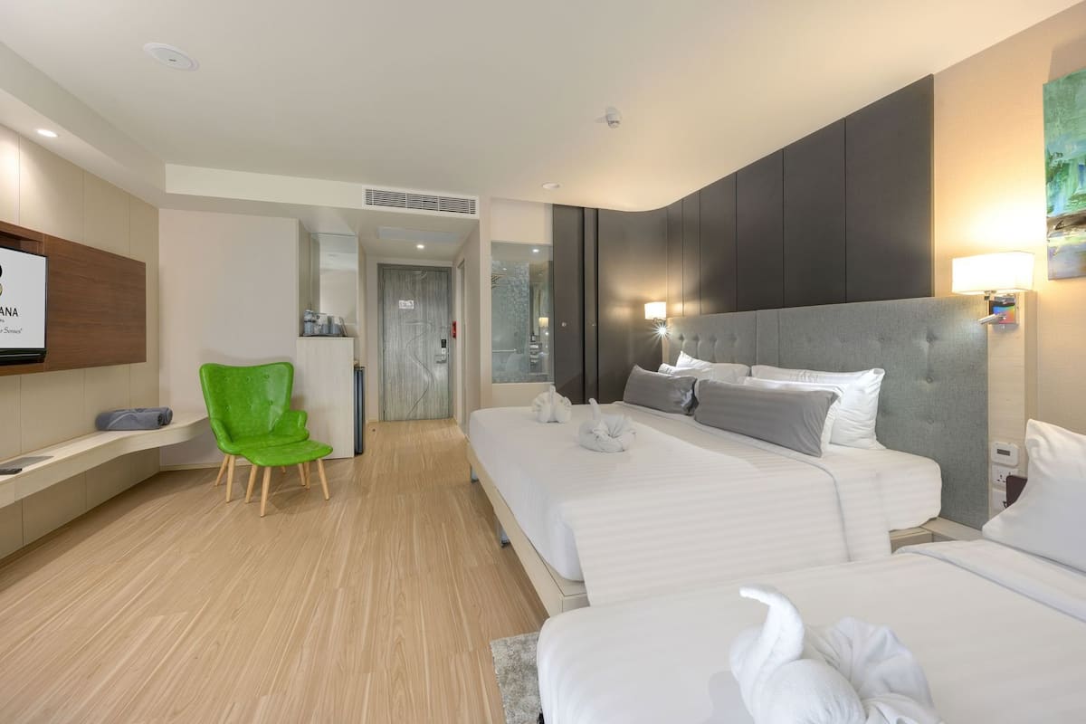 Quarto de hotel com duas camas, uma cadeira verde, televisão e banheiro visível através de uma porta.
