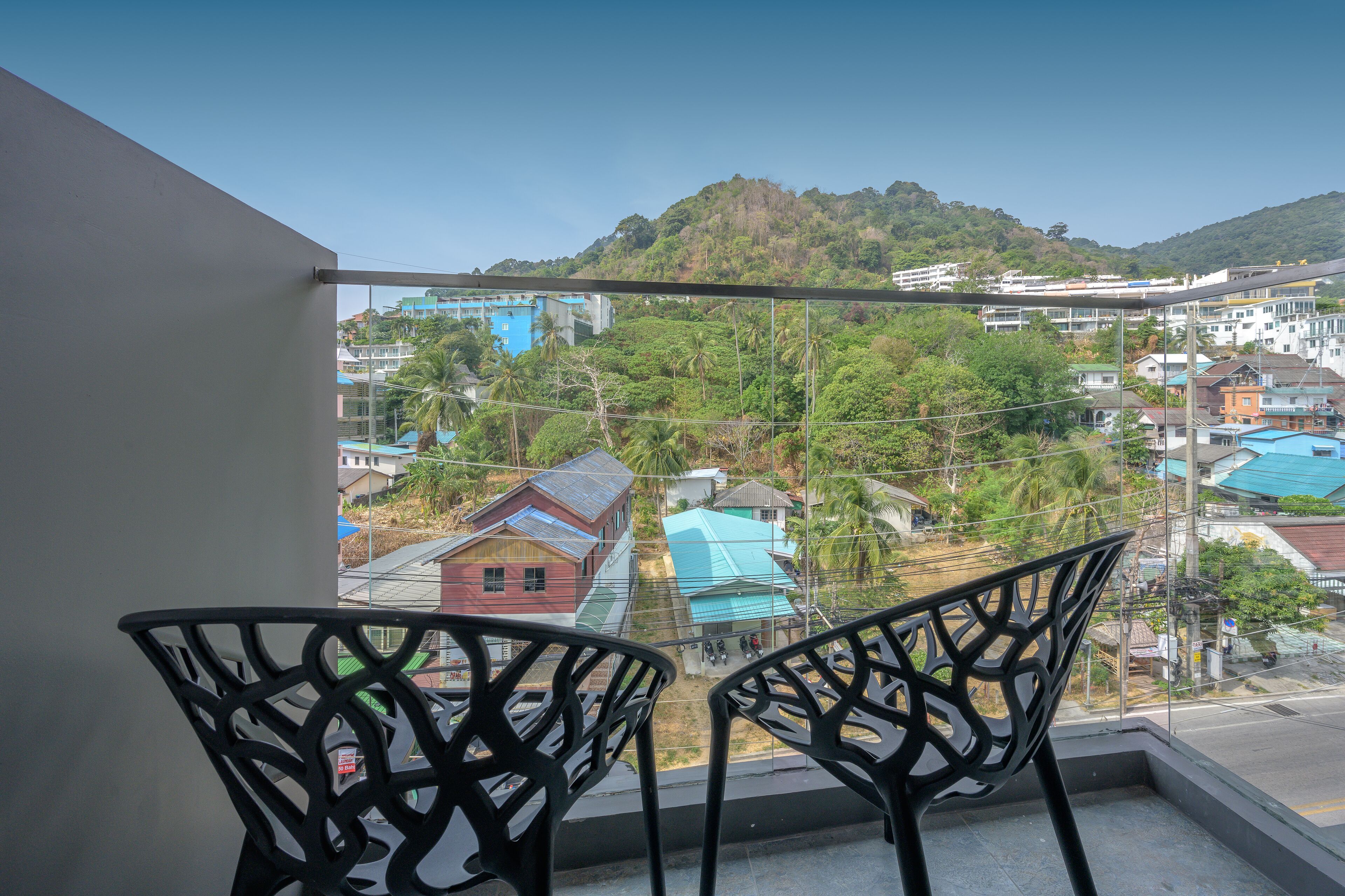 Uma varanda com duas cadeiras, vista para uma área residencial e uma montanha ao fundo.