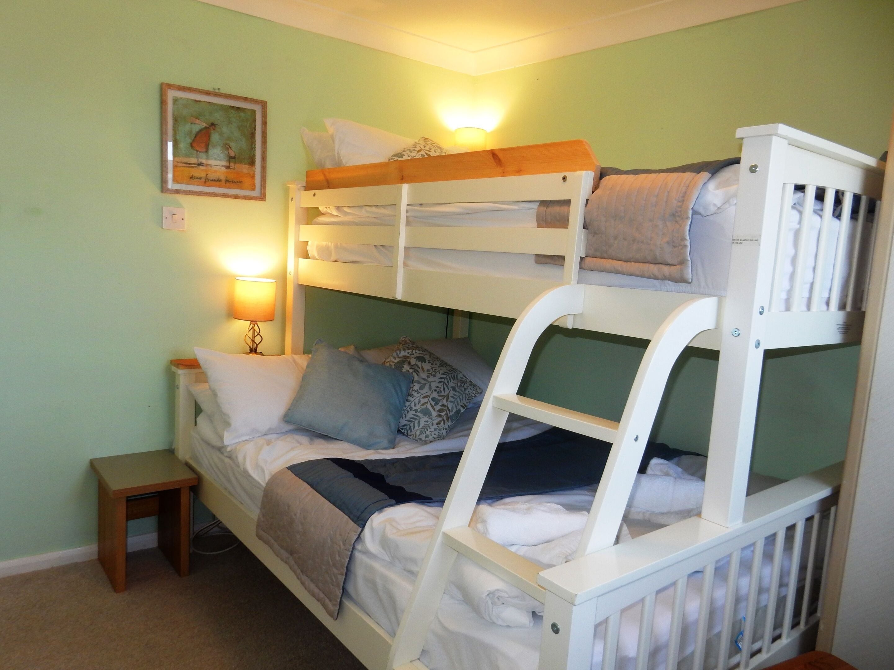Quarto com beliche, uma mesinha de cabeceira e luminária fixada na parede.