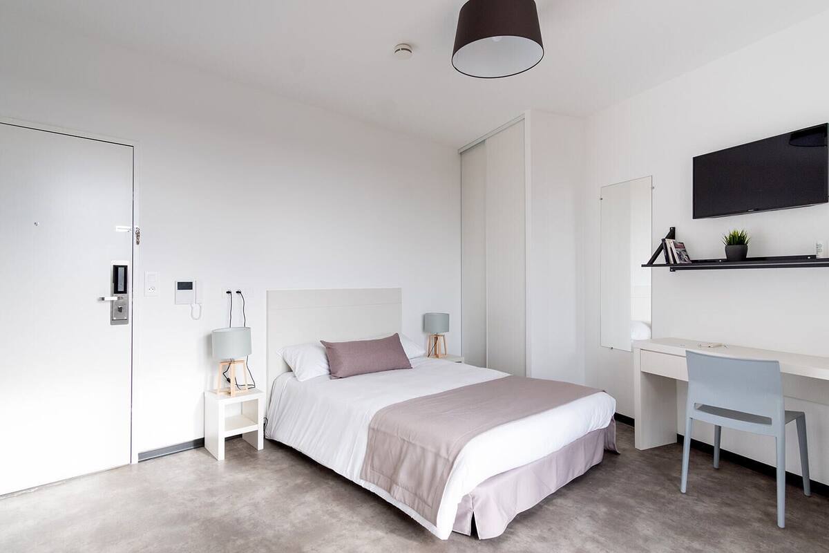 Quarto moderno com cama, mesas de cabeceira, escrivaninha e uma cadeira.