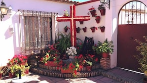 Pátio com uma grande cruz, plantas em vasos e piso de azulejos.