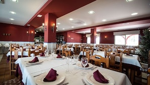 Restaurante com várias mesas preparadas para refeições, com toalhas de mesa brancas e cadeiras de madeira.