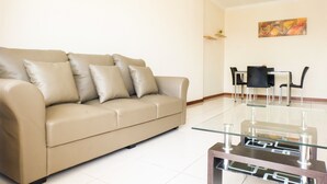 Uma sala de estar com sofá bege, mesa de centro de vidro e uma área de jantar com mesa e cadeiras.