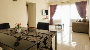Uma sala de estar com sofá, televisão, mesa de jantar com cadeiras e um vaso de planta.