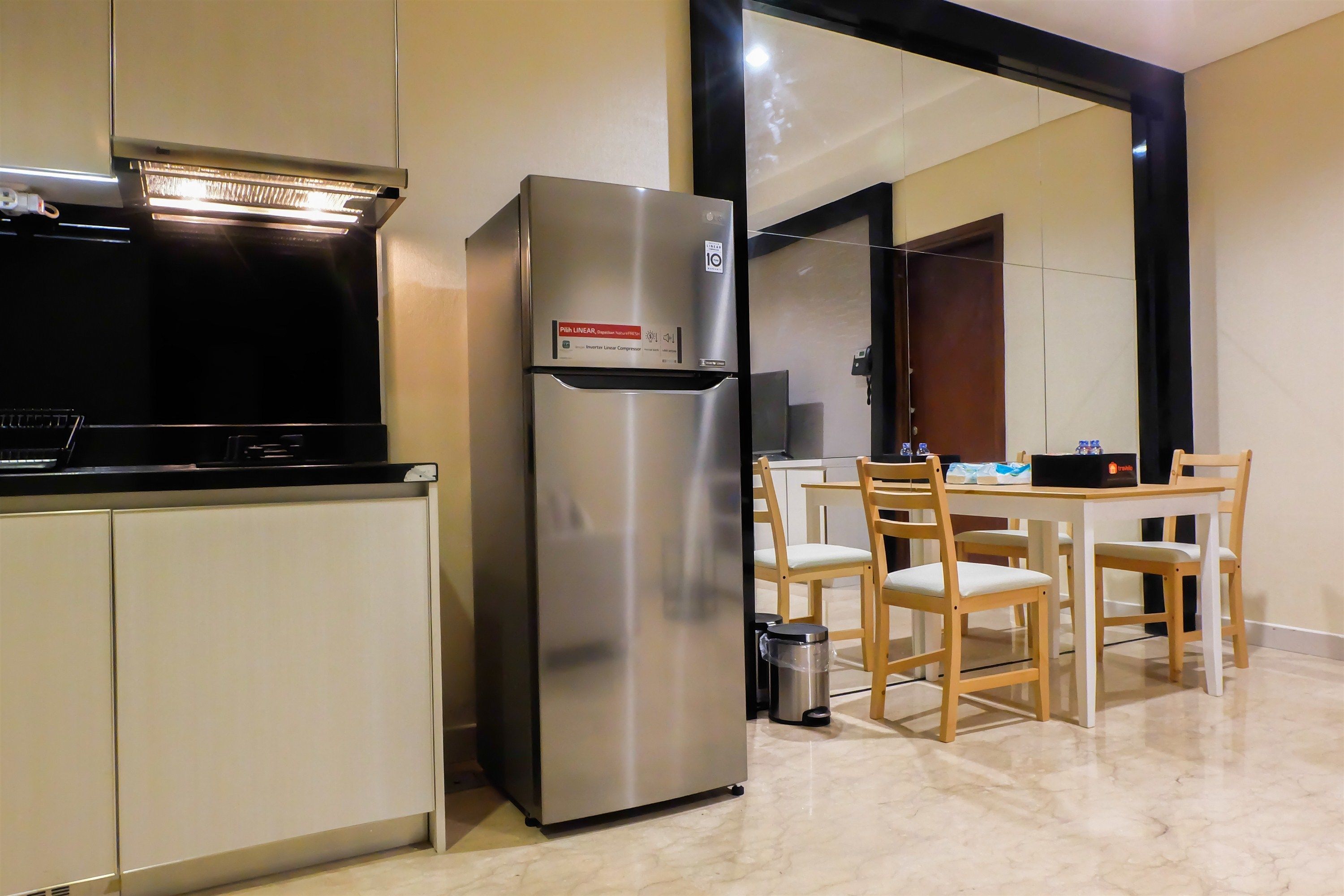Uma cozinha moderna com geladeira de aço inoxidável, micro-ondas e forno embutido. Há uma mesa de jantar com quatro cadeiras e uma lixeira.
