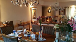 Uma sala de jantar com uma mesa redonda posta para uma refeição, lareira e um candelabro.
