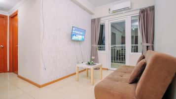 Sala de estar com sofá, televisão na parede, uma mesinha com uma planta e porta de vidro deslizante para uma varanda.