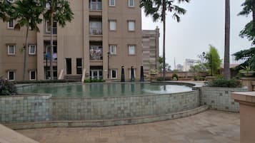 Edifício residencial com piscina, palmeiras e um caminho com azulejos.