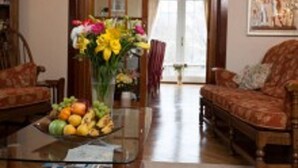 Uma sala de estar com uma mesa de centro de vidro, um arranjo de flores e uma cesta de frutas.