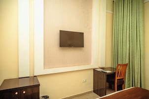 Quarto de hotel com televisão de tela plana na parede, escrivaninha de madeira, uma cadeira e uma cama.