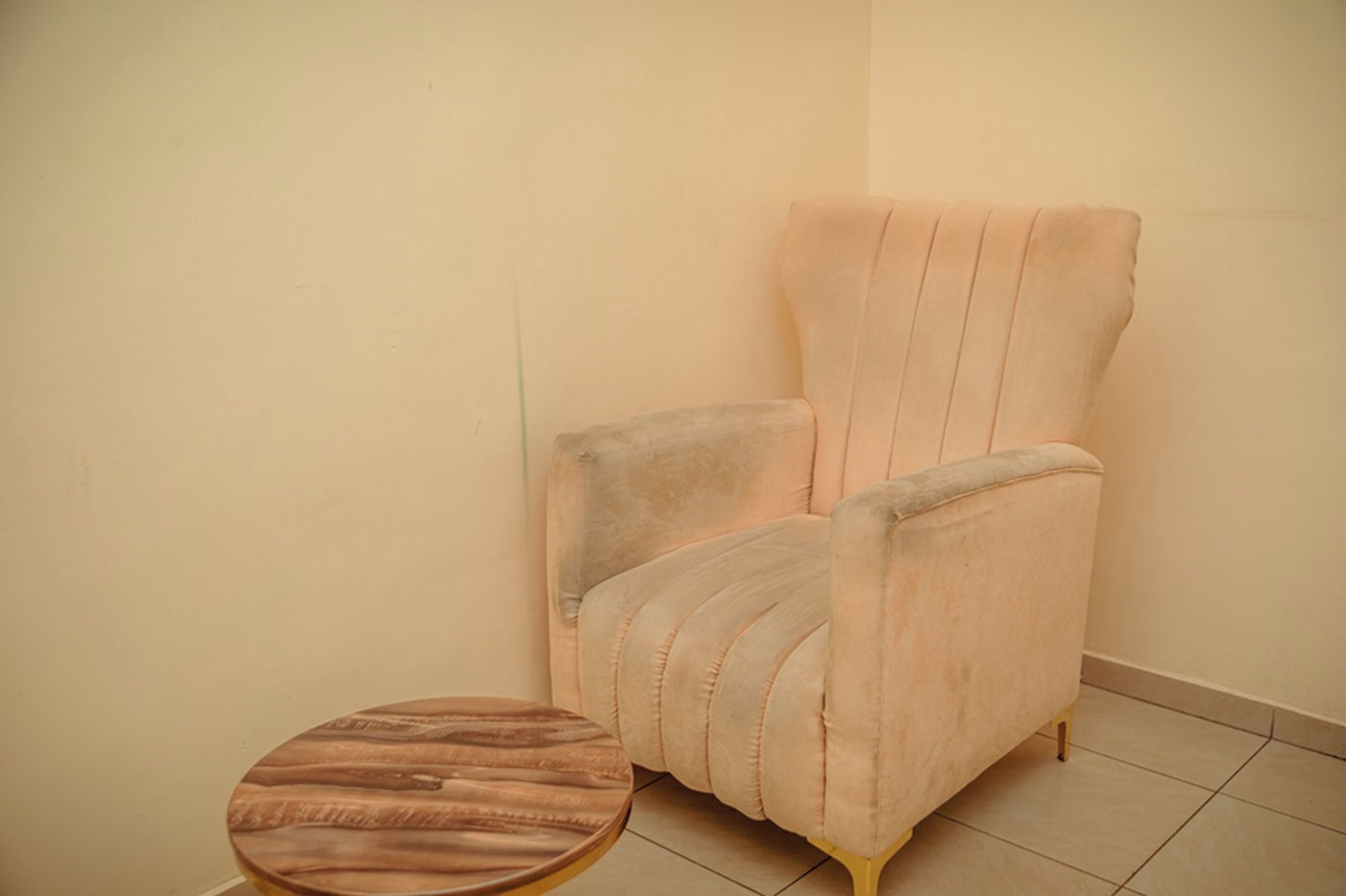 Quarto de canto com poltrona clara e uma mesinha redonda.
