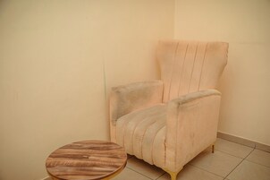 Quarto de canto com poltrona clara e uma mesinha redonda.