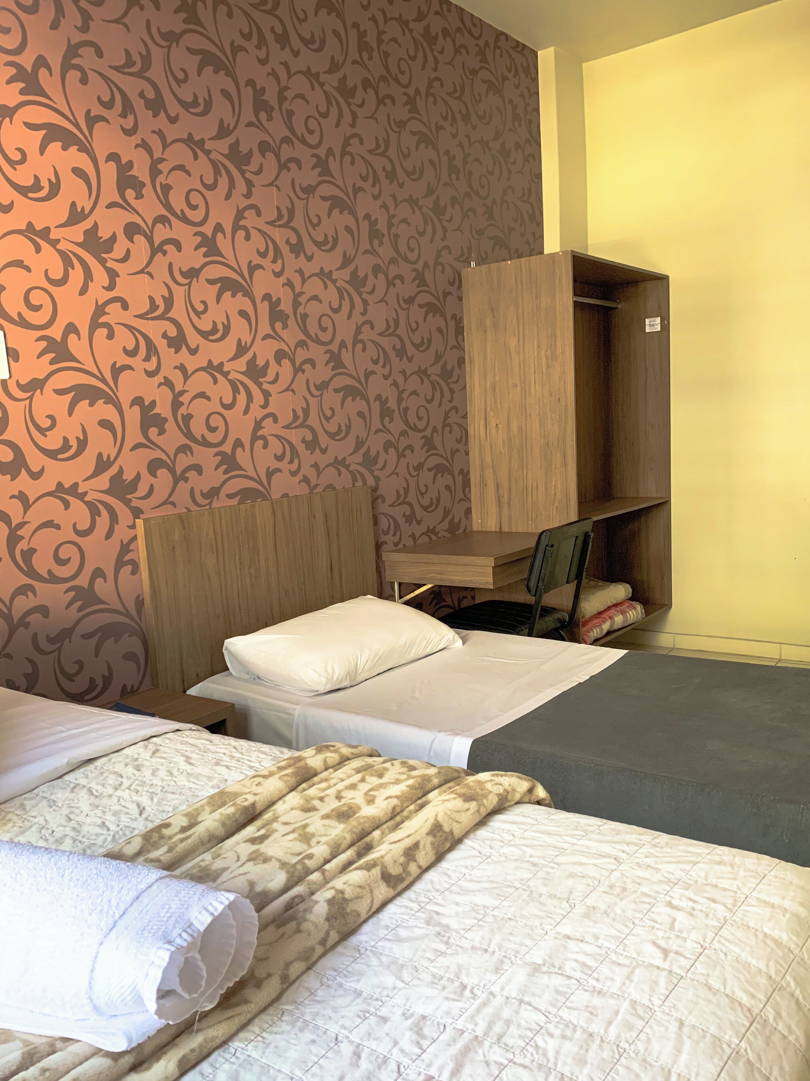 Quarto de hotel com duas camas, uma escrivaninha e um guarda-roupa.