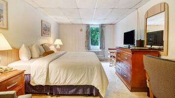 Quarto de hotel com cama, luminárias de cabeceira, escrivaninha com televisão, uma cadeira e um espelho grande.