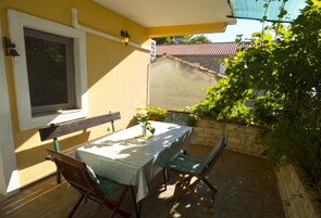Um pátio com mesa e cadeiras, uma janela e vista de um edifício com telhado cerâmico.